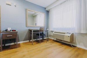 Quarto com escrivaninha, cadeira, espelho e janela com cortinas.