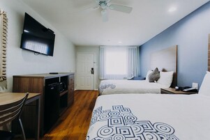 Quarto de hotel com cama, mesa de cabeceira, televisão e escrivaninha com cadeira.