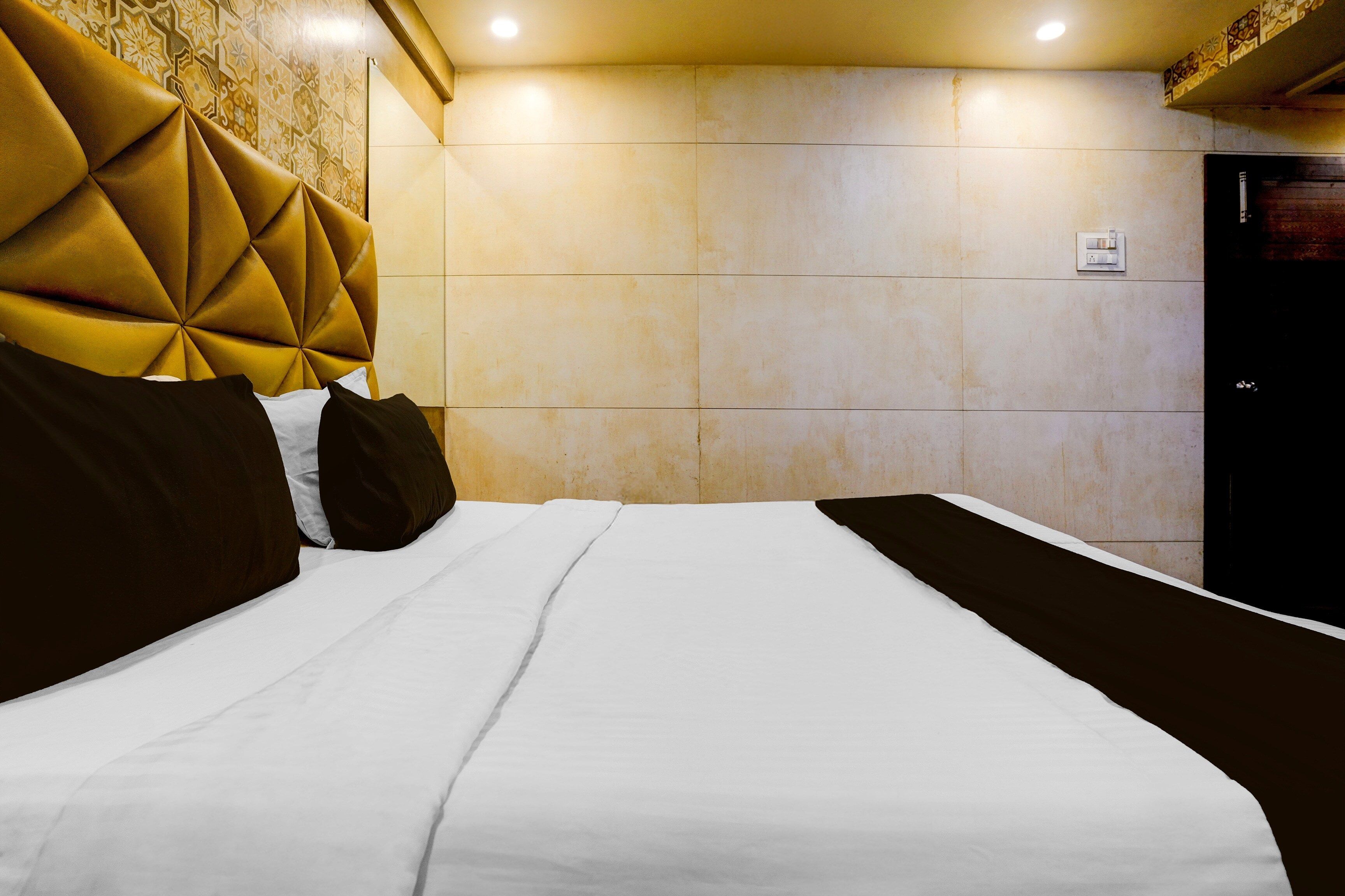 Quarto de hotel com uma cama grande, cabeceira com padrão geométrico e parede revestida em azulejos.