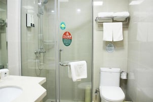 Um banheiro com chuveiro em gabinete de vidro, vaso sanitário e pia. Toalhas penduradas em um suporte e um dispensador de sabonete na parede.