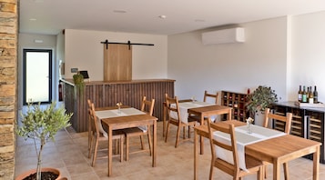 Um restaurante com mesas e cadeiras de madeira, um espaço de bar com garrafas de vinho e uma pequena planta em vaso.