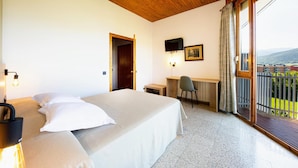 Quarto de hotel com cama, escrivaninha, poltrona, televisão e varanda com vista.