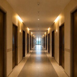 Corredor de hotel longo e bem iluminado, com portas nos dois lados que dão acesso a quartos individuais.