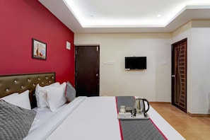 Quarto de hotel com cama, televisão e cafeteira no criado-mudo.