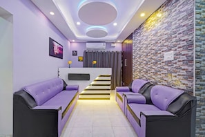 Interior moderno com balcão de recepção, sofás roxos, escada e parede estampada.