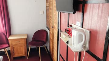 Quarto pequeno com televisão na parede, uma cadeira vermelha, um armário de madeira e um radiador.