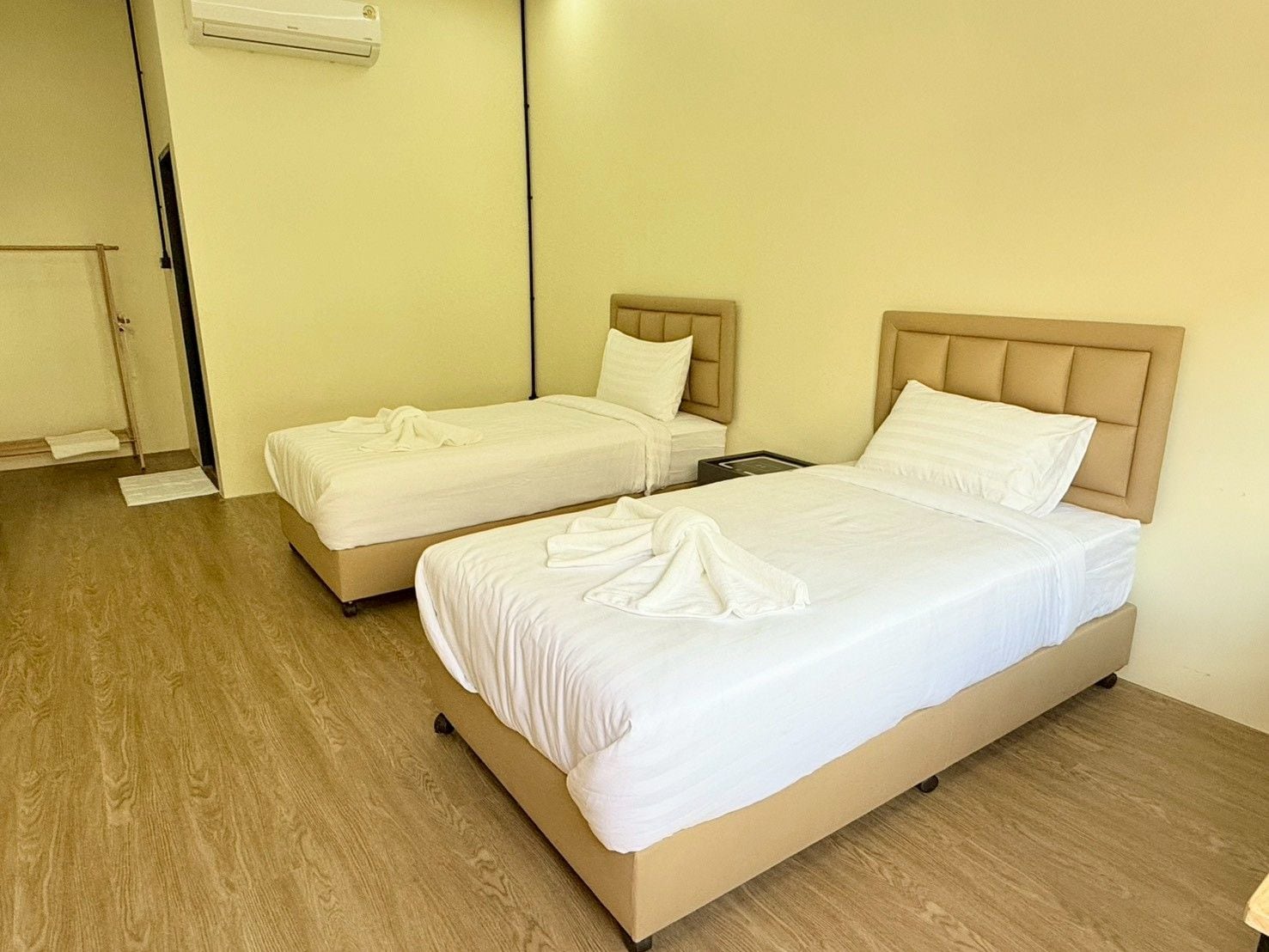 Quarto de hotel com duas camas, piso de madeira, ar condicionado fixado na parede e uma porta.