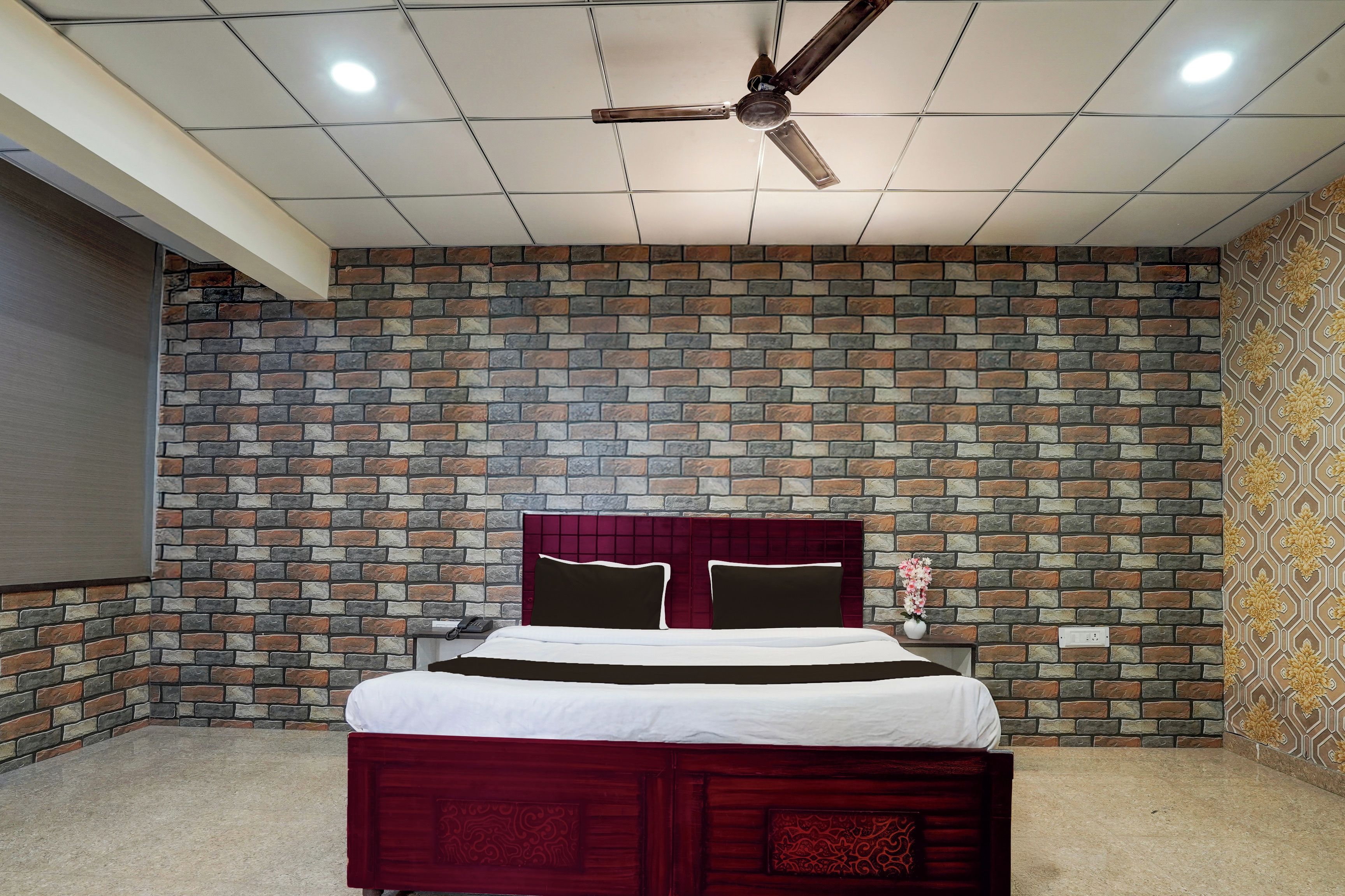 Quarto com parede de tijolos, cama com cabeceira escura e ventilador de teto.