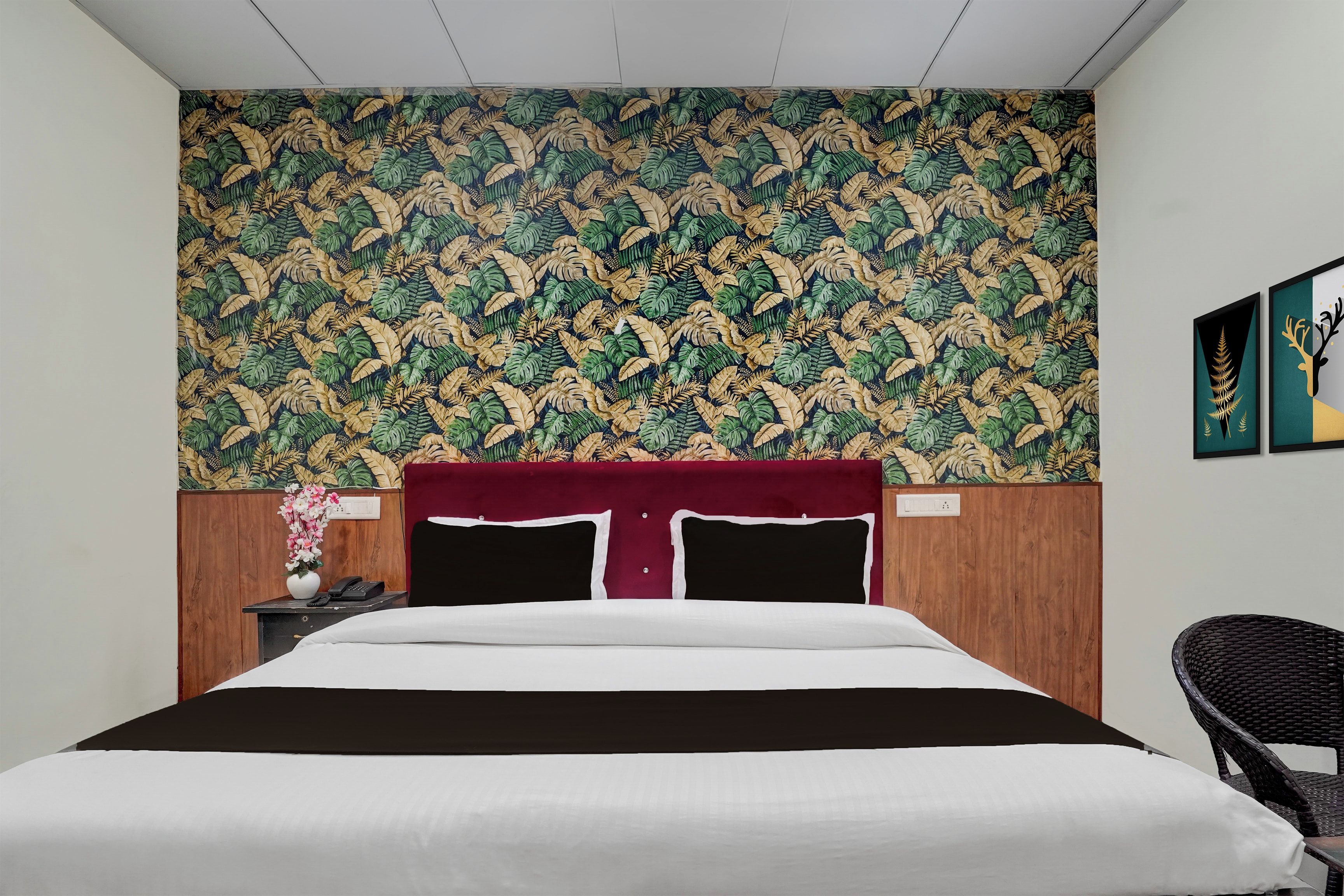 Quarto de hotel com cama, mesa de cabeceira, poltrona e parede com padrão de folhagem.