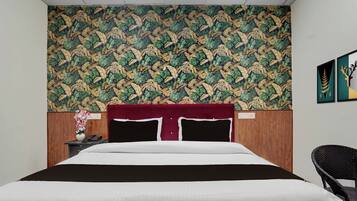 Quarto de hotel com cama, mesa de cabeceira, poltrona e parede com padrão de folhagem.