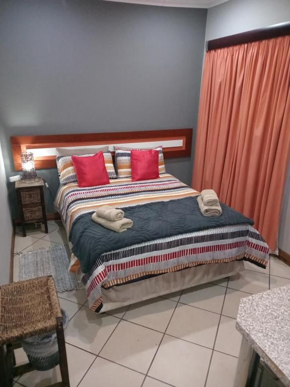 Quarto com cama, travesseiros, mesa de cabeceira, cadeira e janela com cortinas.