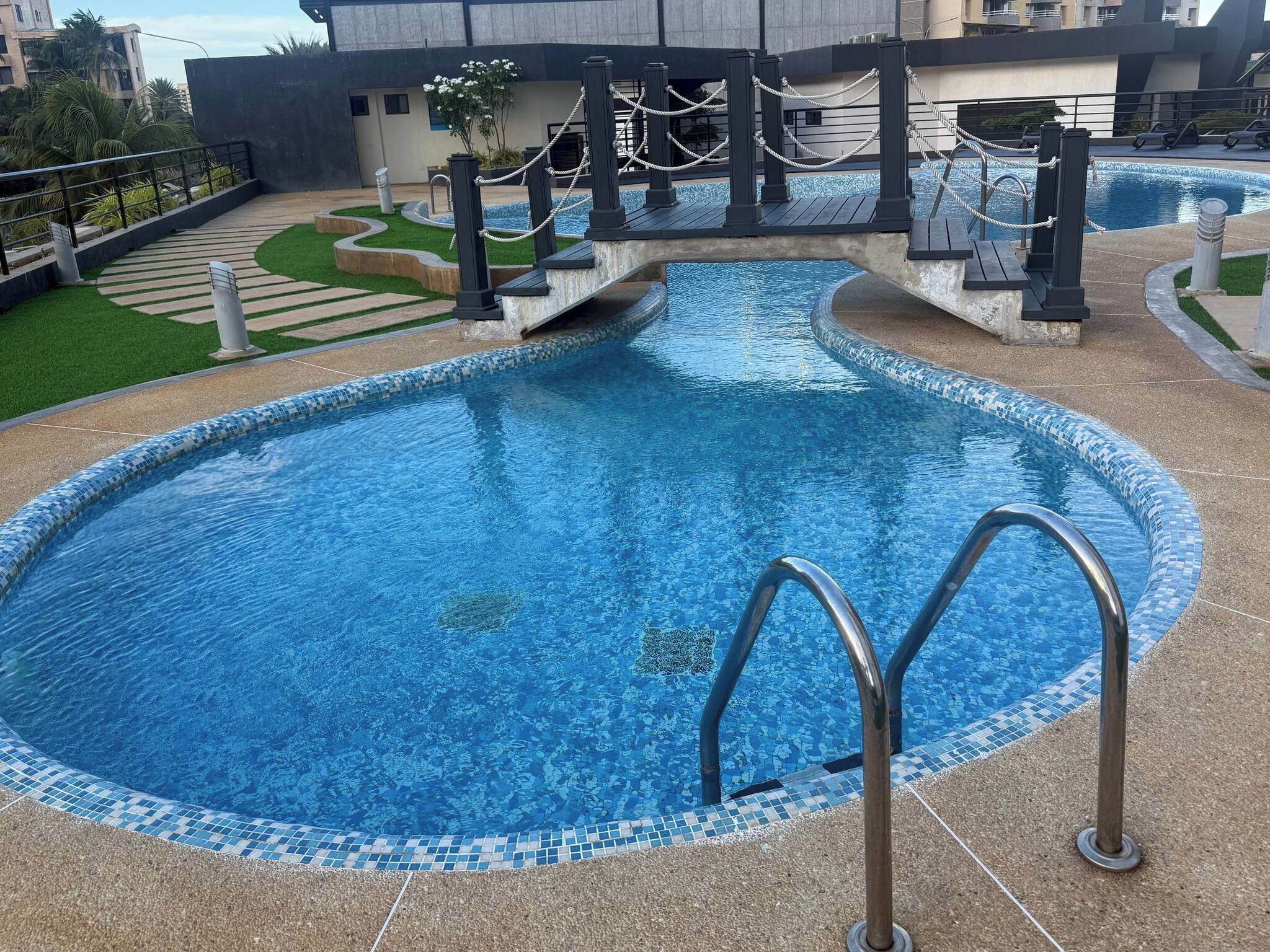 Piscina com borda revestida, cercada por área de deck com barreira de corda.