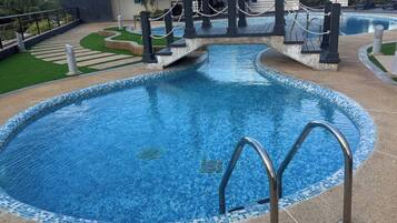 Piscina com borda revestida, cercada por área de deck com barreira de corda.