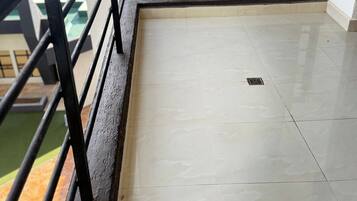 Uma varanda com grade de metal, piso de azulejos e vista de um prédio ao fundo.