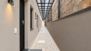 Um corredor com piso de azulejos, uma porta preta com número e um luminário fixado na parede.
