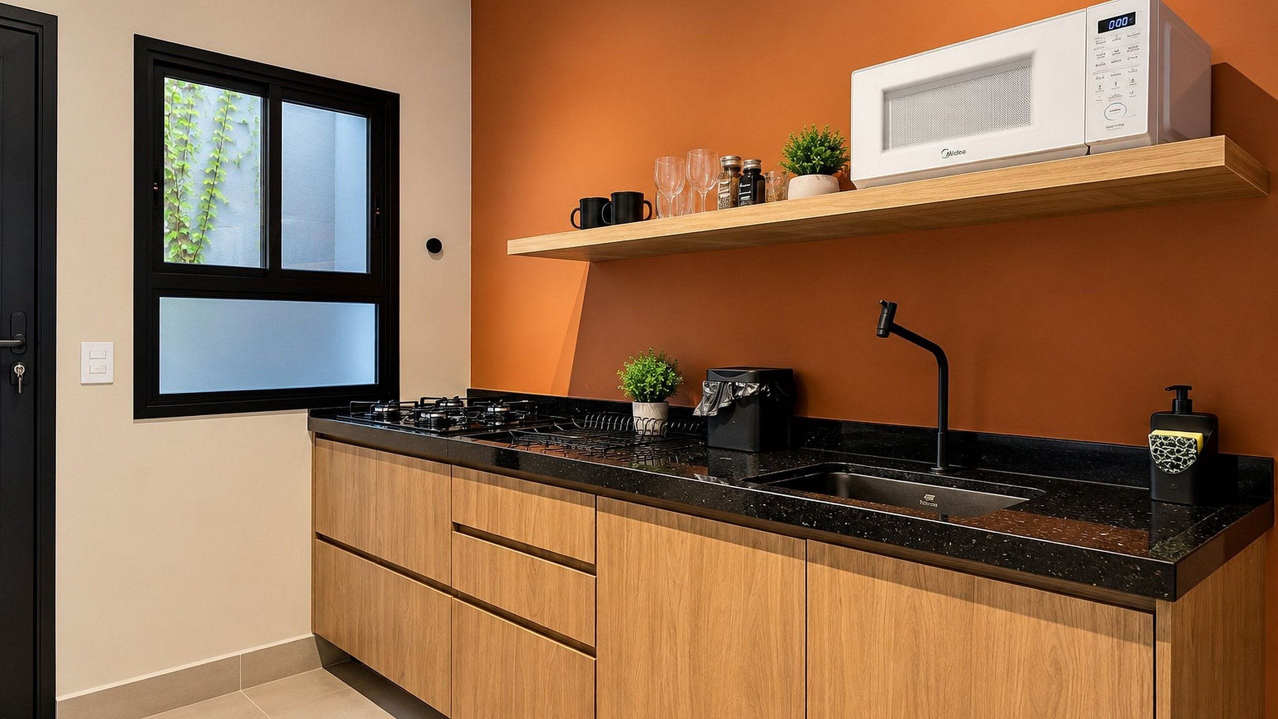 Cozinha moderna com bancada preta, armários de madeira, micro-ondas e janela com vista para o verde.
