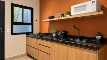 Cozinha moderna com bancada preta, armários de madeira, micro-ondas e janela com vista para o verde.