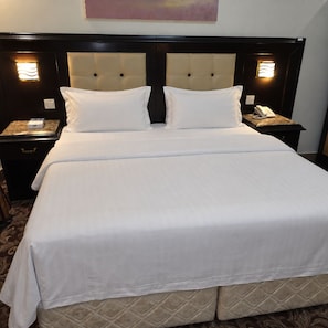 Quarto de hotel com uma cama grande, duas mesas de cabeceira, um telefone fixado na parede e um quadro sobre a cama.