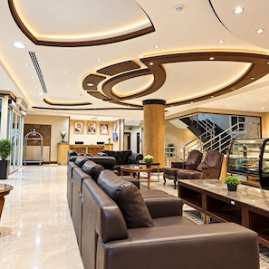 Um lobby moderno com balcão de atendimento, assentos de couro, escada e piso de mármore.