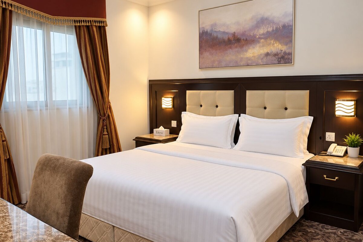 Quarto de hotel com uma cama grande, mesa de cabeceira com abajur, uma cadeira e um quadro na parede.