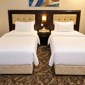 Quarto de hotel com duas camas, uma mesa de cabeceira com abajur e um tapete estampado.