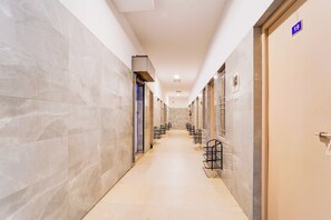Corredor de hotel com paredes de mármore, chão em mosaico e portas identificadas com números de quarto.