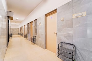 Corredor de hotel com paredes de mármore, portas numeradas e prateleiras de metal para armazenamento.