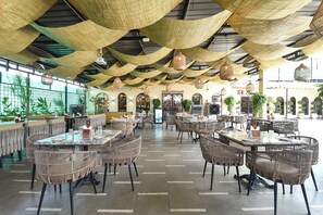 Uma área de refeições interna com móveis de vime, mesas e luminárias pendentes.