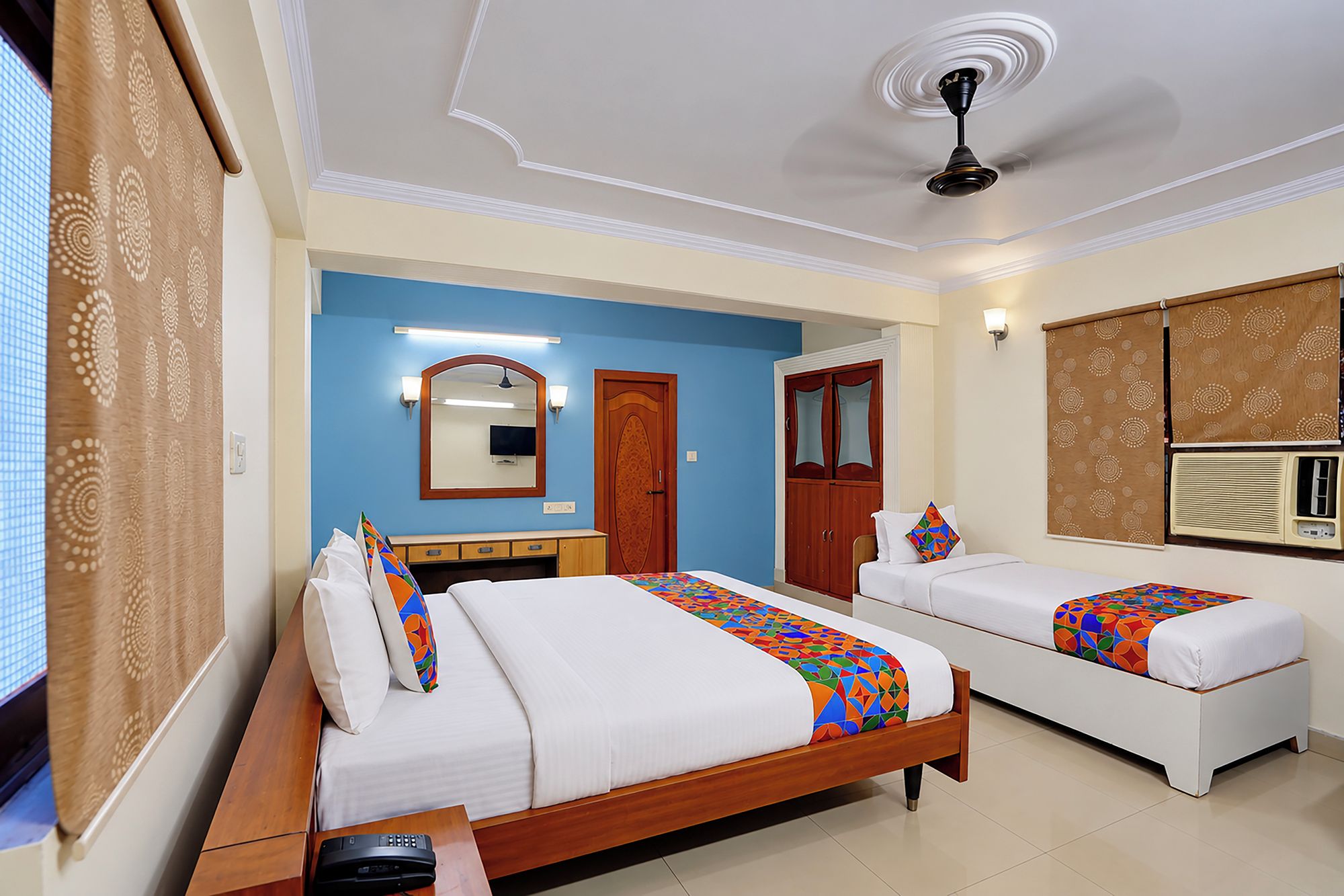 Quarto de hotel com duas camas, um ventilador de teto, um espelho e uma janela com persianas.