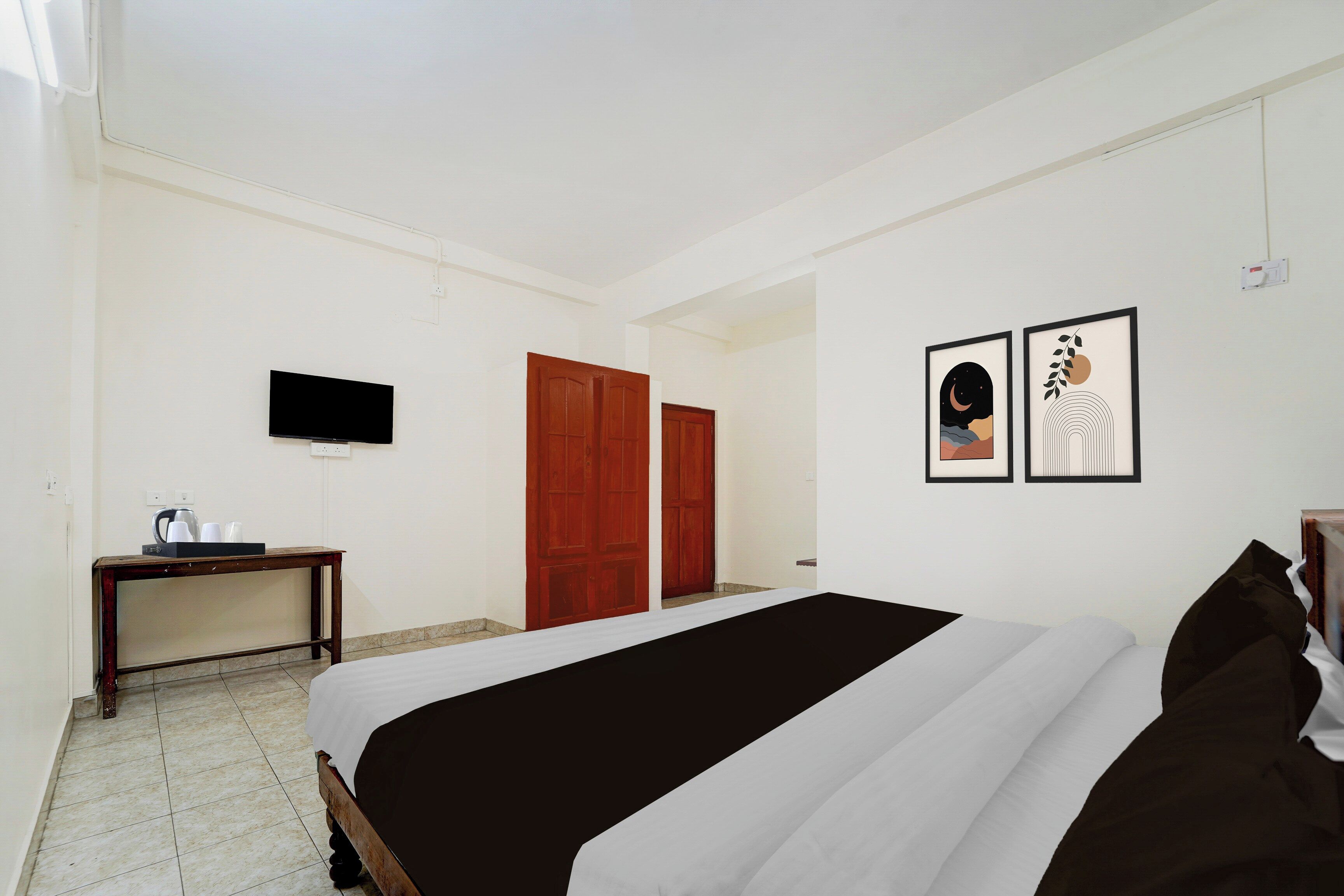 Quarto de hotel com cama, televisão, escrivaninha com chaleira e duas portas.