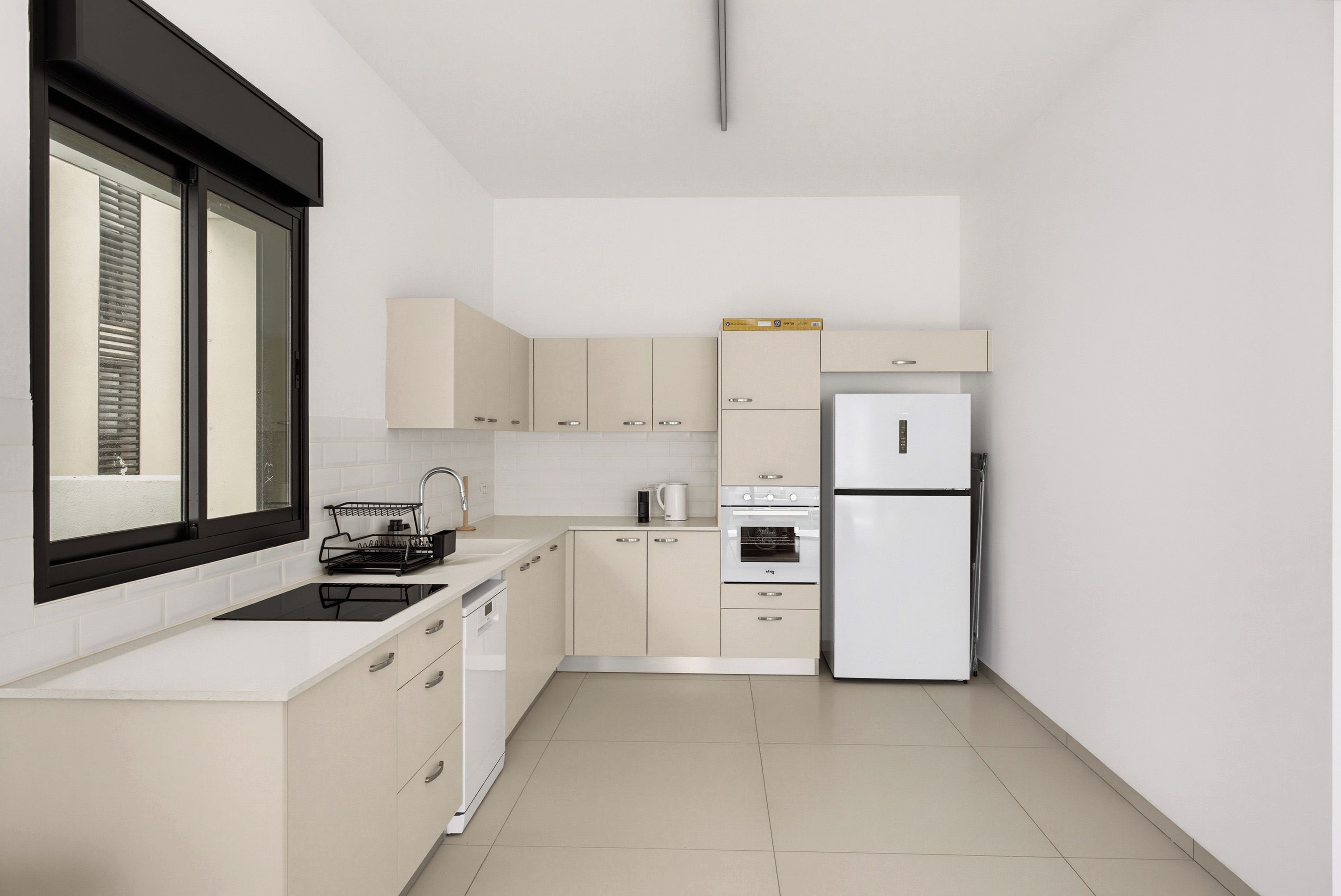 Cozinha compacta com armários brancos, bancada preta, forno embutido e geladeira.