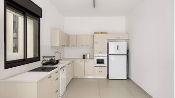 Cozinha compacta com armários brancos, bancada preta, forno embutido e geladeira.