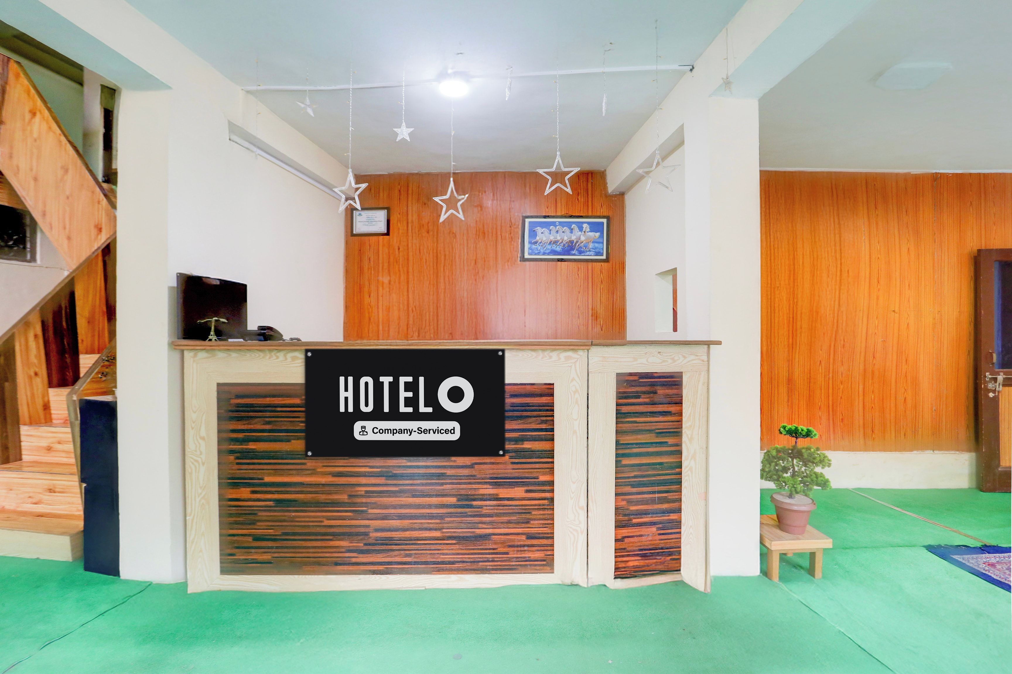 Bancada de recepção com uma placa indicando 'HOTEL' e um símbolo de serviço da empresa. Há uma moldura com um quadro acima da bancada e um enfeite de estrela no teto.