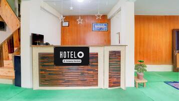 Bancada de recepção com uma placa indicando 'HOTEL' e um símbolo de serviço da empresa. Há uma moldura com um quadro acima da bancada e um enfeite de estrela no teto.