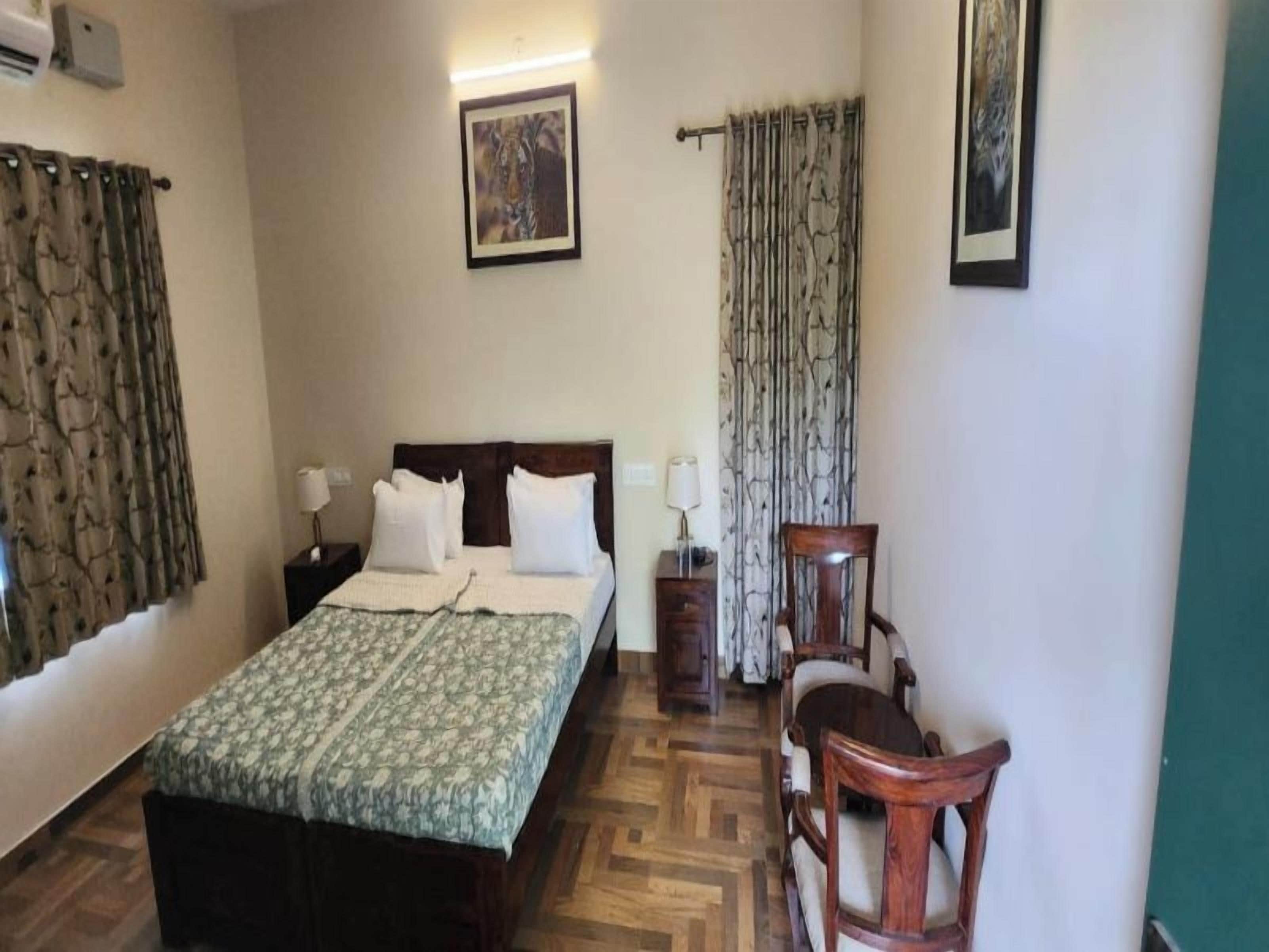 Quarto de hotel com cama, mesas de cabeceira, uma cadeira e cortinas.