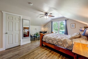 Quarto com cama, ventoinha no teto, escrivaninha, cadeira e janela com cortinas.