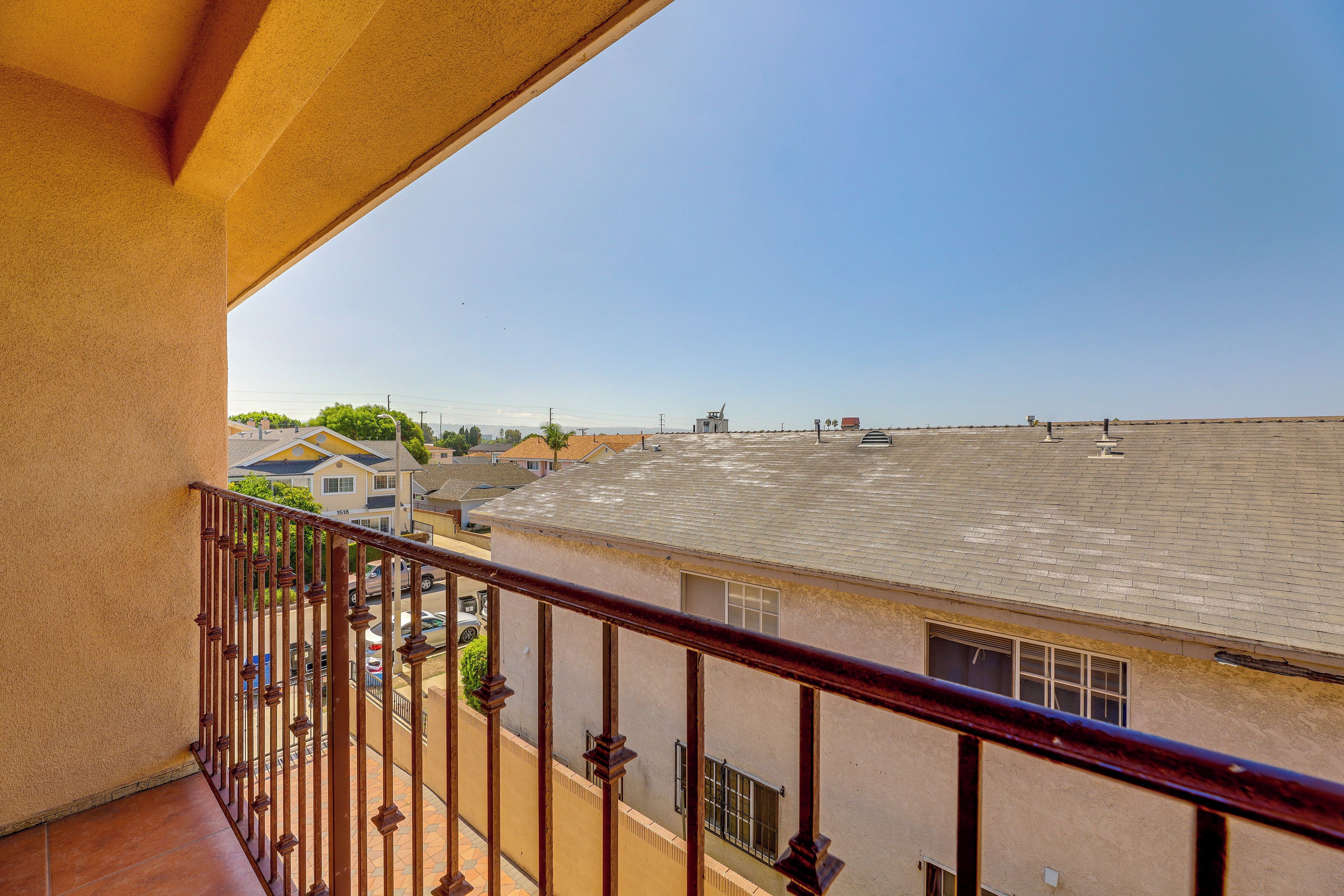 Uma varanda com vista para uma área residencial, incluindo casas e uma grande estrutura com telhado plano.