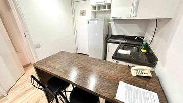 Cozinha compacta com mesa de madeira, duas cadeiras pretas, geladeira branca e bancada preta.