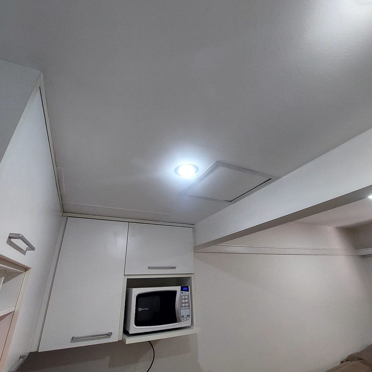 Uma cozinha compacta com micro-ondas embutido, armários brancos e luminária no teto.