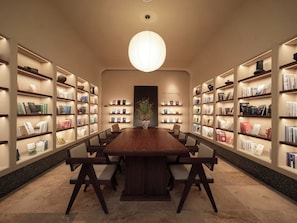 Uma biblioteca com uma longa mesa de madeira e cadeiras, cercada por estantes repletas de livros.