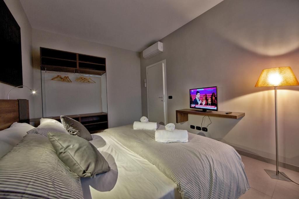 Quarto de hotel com uma cama, televisão, luminária e prateleira com toalhas.