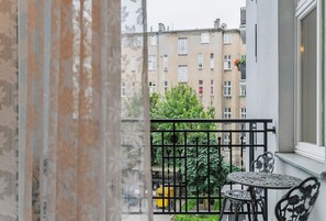 Uma varanda com vista para um edifício, uma mesa pequena e cadeiras.