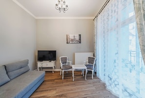 Sala de estar com sofá, televisão, duas cadeiras, mesa e radiador.