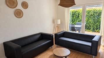 Uma sala de estar moderna com dois sofás pretos, uma pequena mesa de madeira e um candeeiro suspenso.