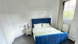 Quarto com cama, mesa de cabeceira, janela com cortinas e radiador.