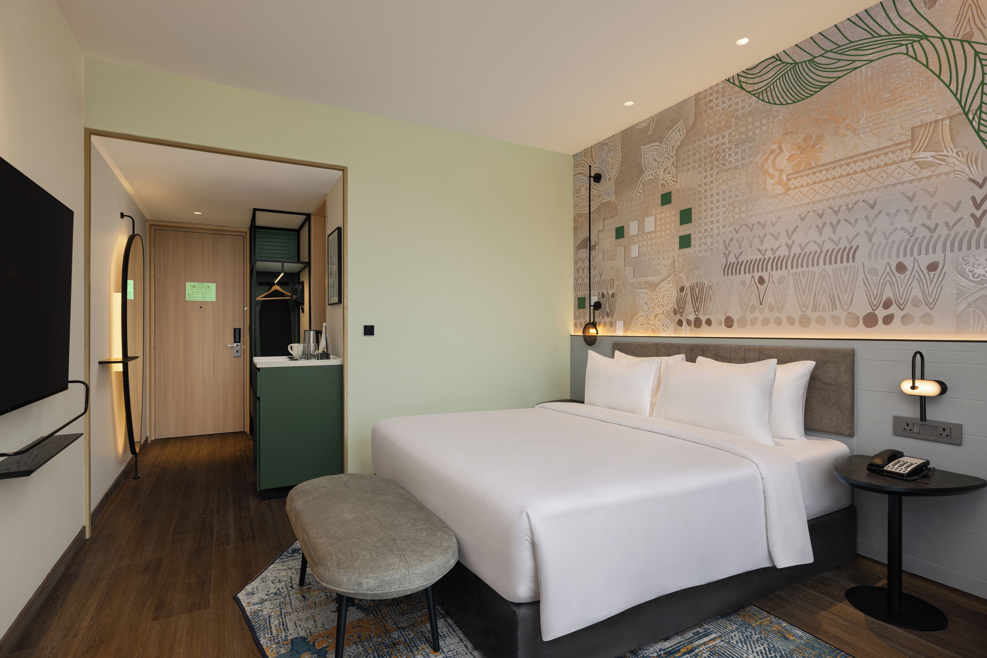 Quarto de hotel com cama, escrivaninha, cadeira, telefone e televisão na parede.