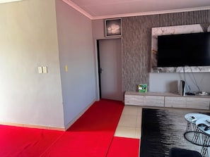 Uma sala de estar moderna com televisão de tela plana na parede, um móvel de entretenimento de madeira e um tapete vermelho.