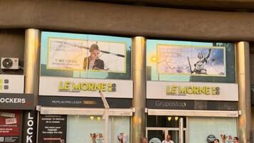 Um edifício com fachada comercial identificada como 'LE MORNE' e uma placa de parada de ônibus.