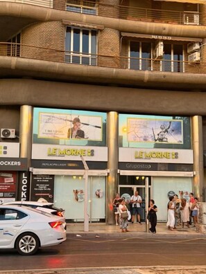 Um edifício com fachada comercial identificada como 'LE MORNE' e uma placa de parada de ônibus.