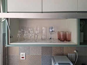 Uma cozinha com uma prateleira exibindo diversos copos, incluindo taças de vinho e copos de vidro.